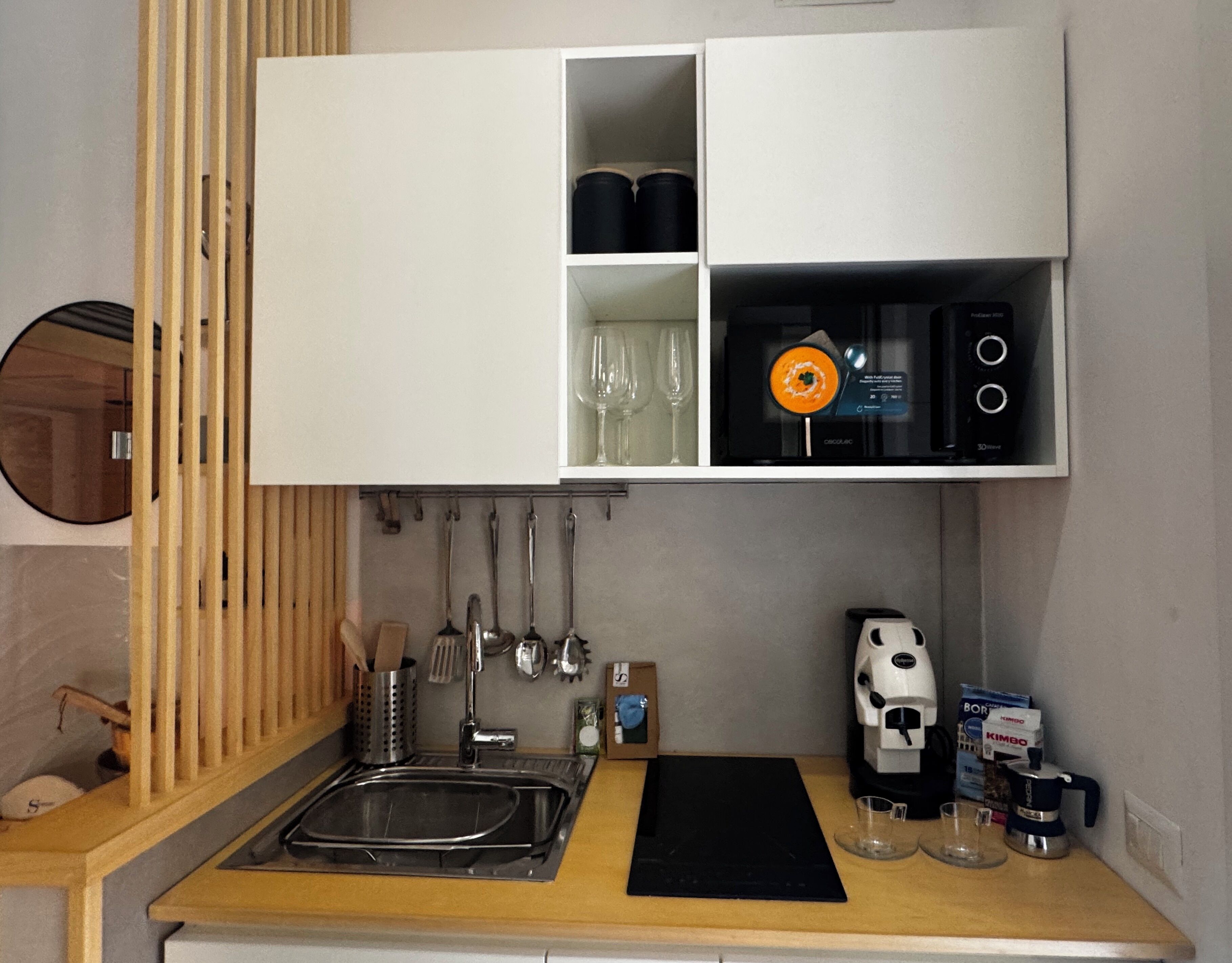 Uma cozinha compacta com micro-ondas embutido, máquina de café e uma pia pequena.