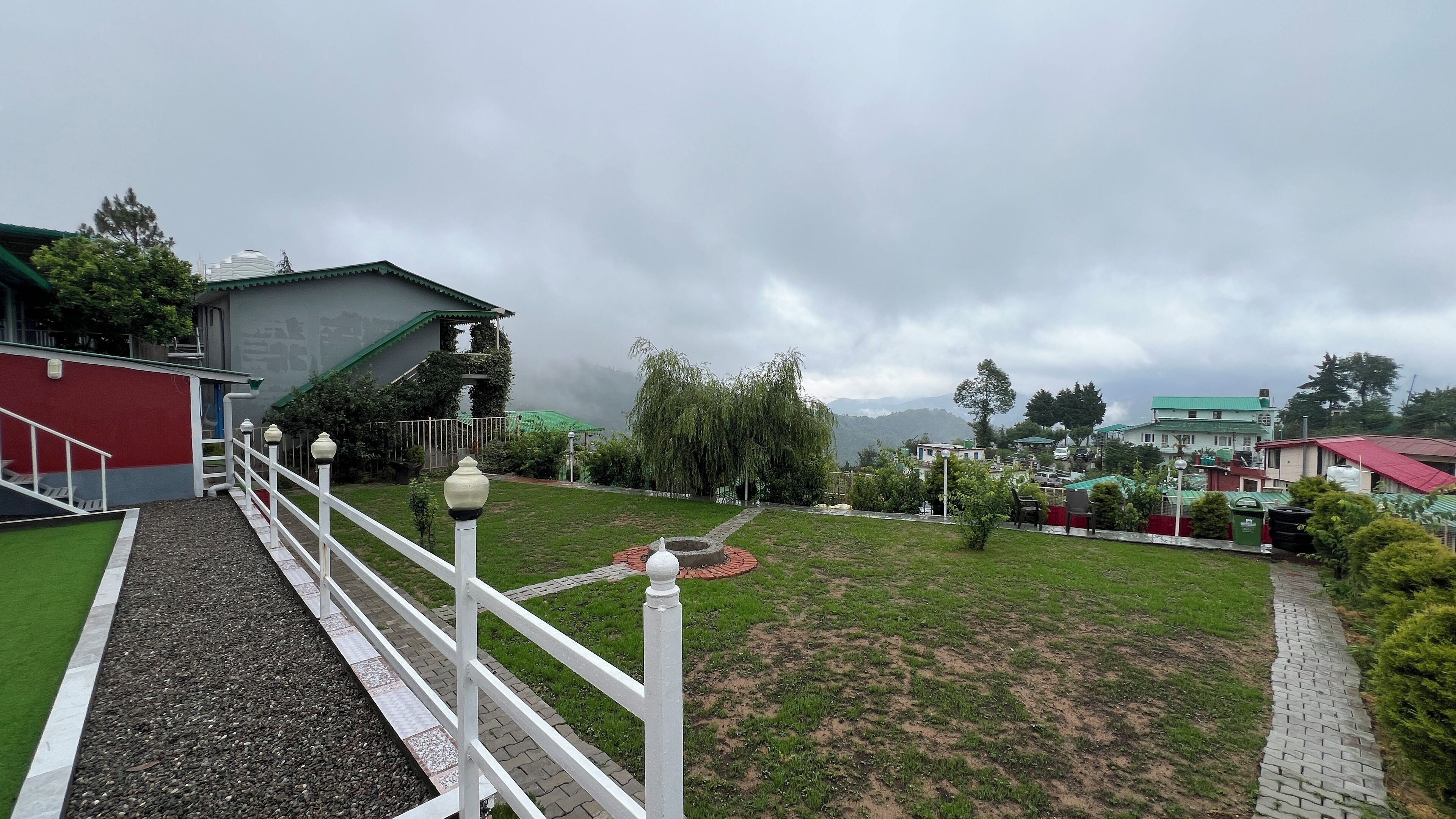 Um bairro residencial com gramado verde, cerca branca e um edifício com telhado vermelho.