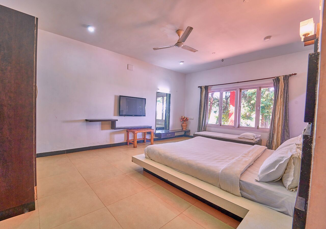 Quarto com cama grande, escrivaninha, televisão e janela com cortinas.