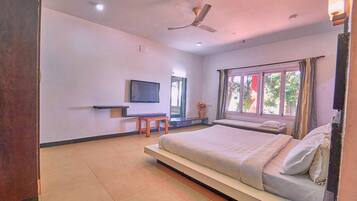 Quarto com cama grande, escrivaninha, televisão e janela com cortinas.