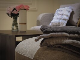 Quarto com sofá, vaso de flores e pilha de toalhas em uma mesa.