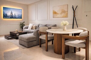 Uma sala de estar moderna com um sofá seccional, uma mesa redonda de madeira com cadeiras, uma TV montada na parede e obras de arte acima do sofá.