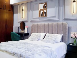 Quarto com cama, mesa de cabeceira, penteadeira, espelho e iluminação na parede.