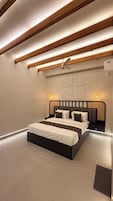 Quarto moderno com cama, vigas de madeira, iluminação embutida, ventoinha no teto e ar condicionado fixado na parede.