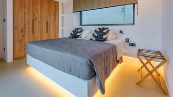 Quarto moderno com cama grande, guarda-roupa de madeira e um espelho fixado na parede.