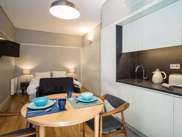 Quarto de hotel compacto com área de refeições, cozinha compacta e uma cama com mesa de cabeceira.
