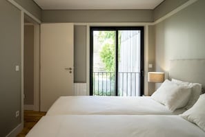 Quarto de hotel com uma cama grande, porta que dá para uma varanda e um abajur na mesa de cabeceira.