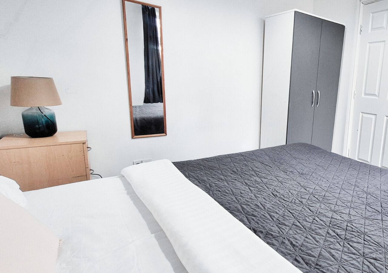 Quarto com cama, mesa de cabeceira com abajur, guarda-roupa e espelho.