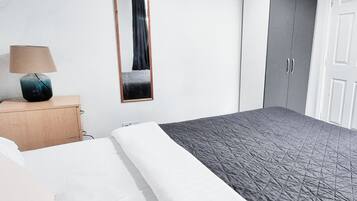 Quarto com cama, mesa de cabeceira com abajur, guarda-roupa e espelho.