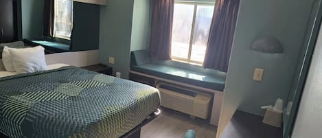Quarto de hotel com cama, escrivaninha e janela com cortinas.