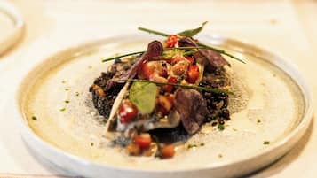 Um prato de comida com diversos ingredientes, incluindo vegetais, tomates e possivelmente carne, sobre um prato de cerâmica.