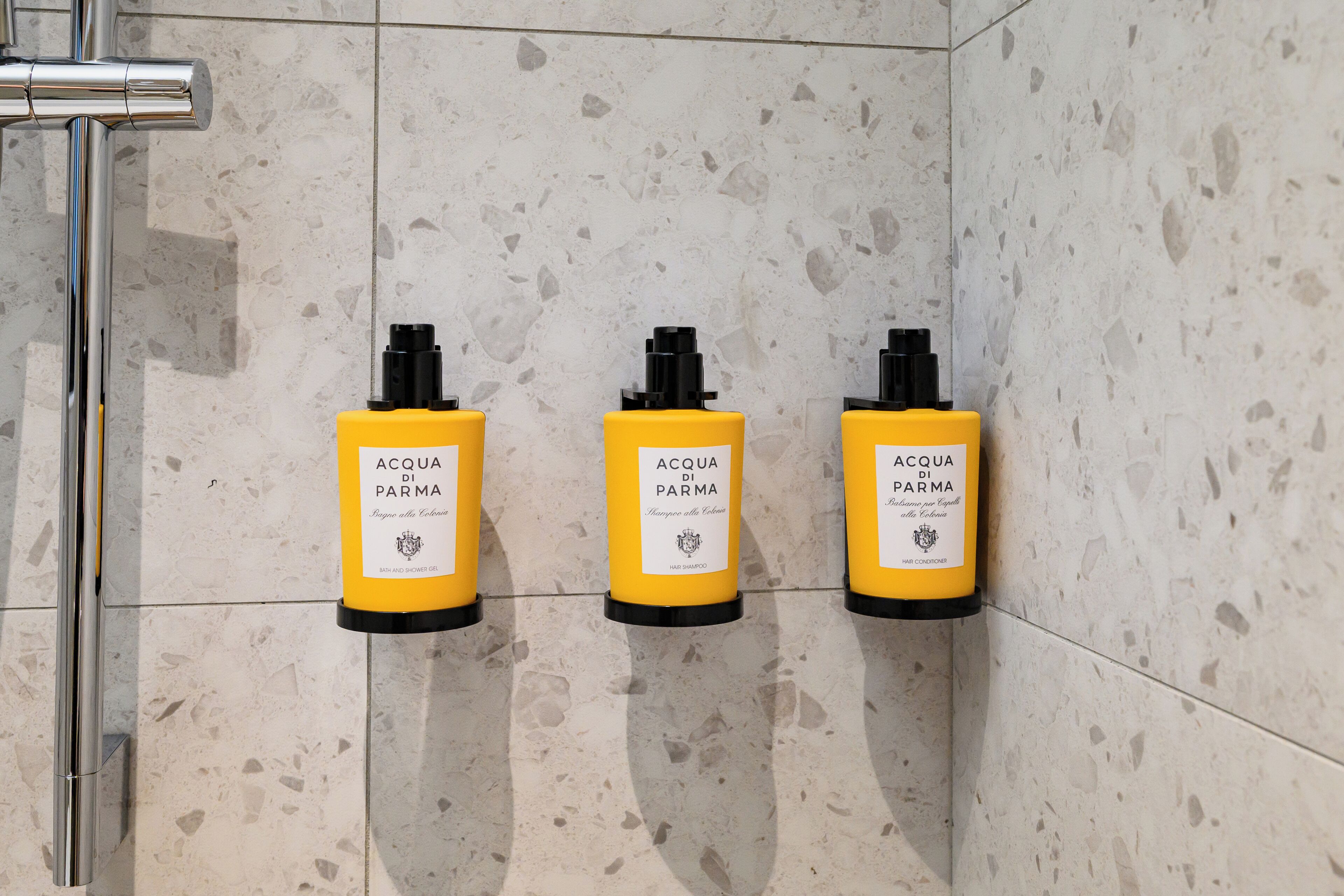Três garrafas de shampoo Acqua di Parma sobre um revestimento de azulejos.