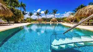 Uma piscina translúcida com espreguiçadeiras e guarda-sóis de palha.