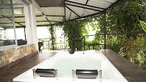 Uma área de spa com uma banheira de hidromassagem grande e retangular, paredes de pedra e vista para o exterior.