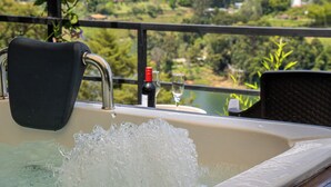 Uma banheira com água corrente, uma garrafa de vinho e um copo numa varanda com vista para uma paisagem deslumbrante.