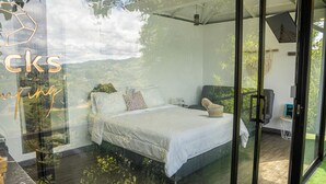 Quarto com cama, mesa de cabeceira e janela com vista para área verde.