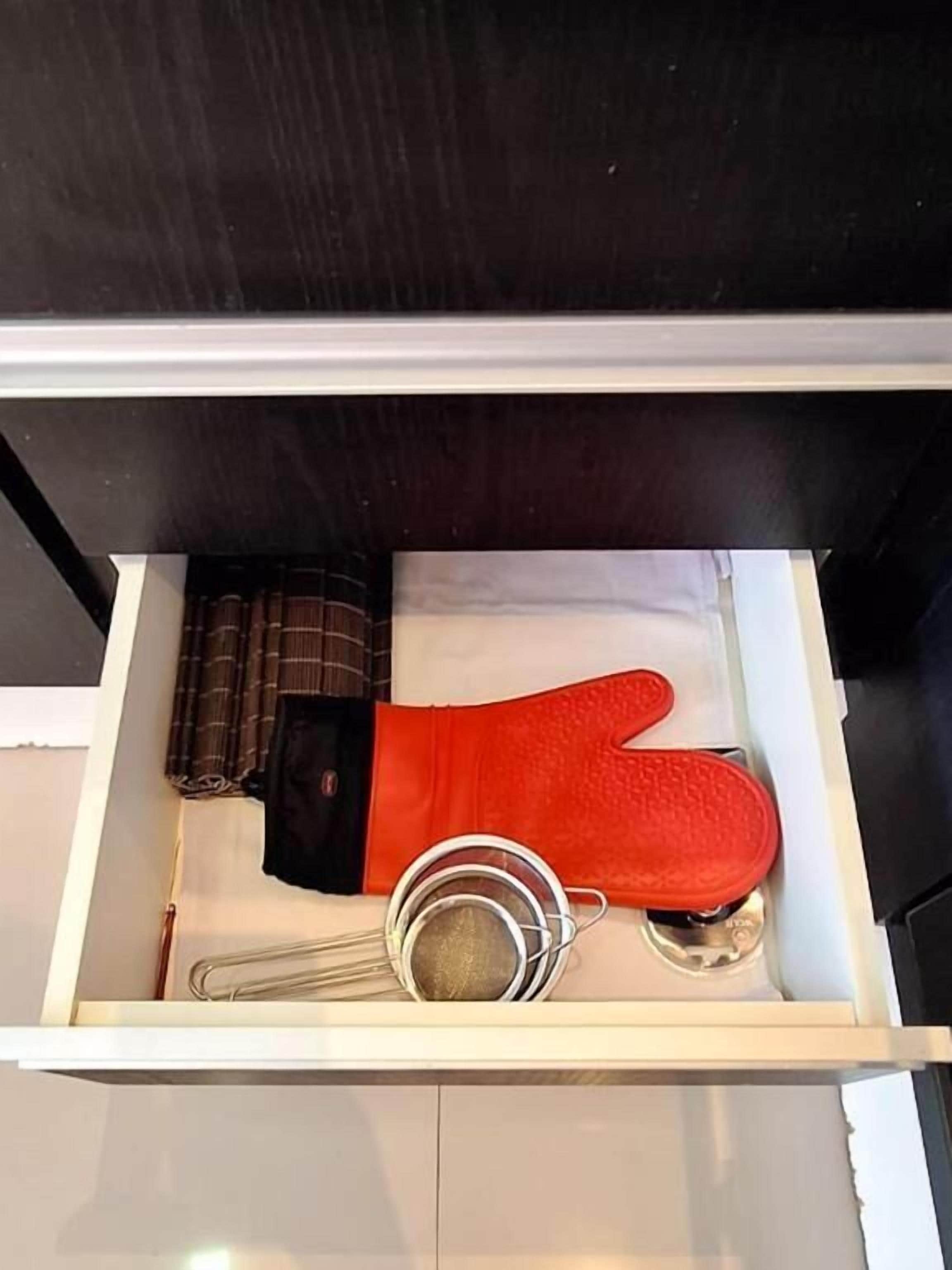 Uma gaveta com uma luva de forno vermelha, um escorredor de metal e um pano xadrez preto e vermelho.