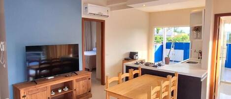 Uma sala de estar moderna com televisão de tela plana, móveis de madeira e uma área de cozinha com mesa e cadeiras.