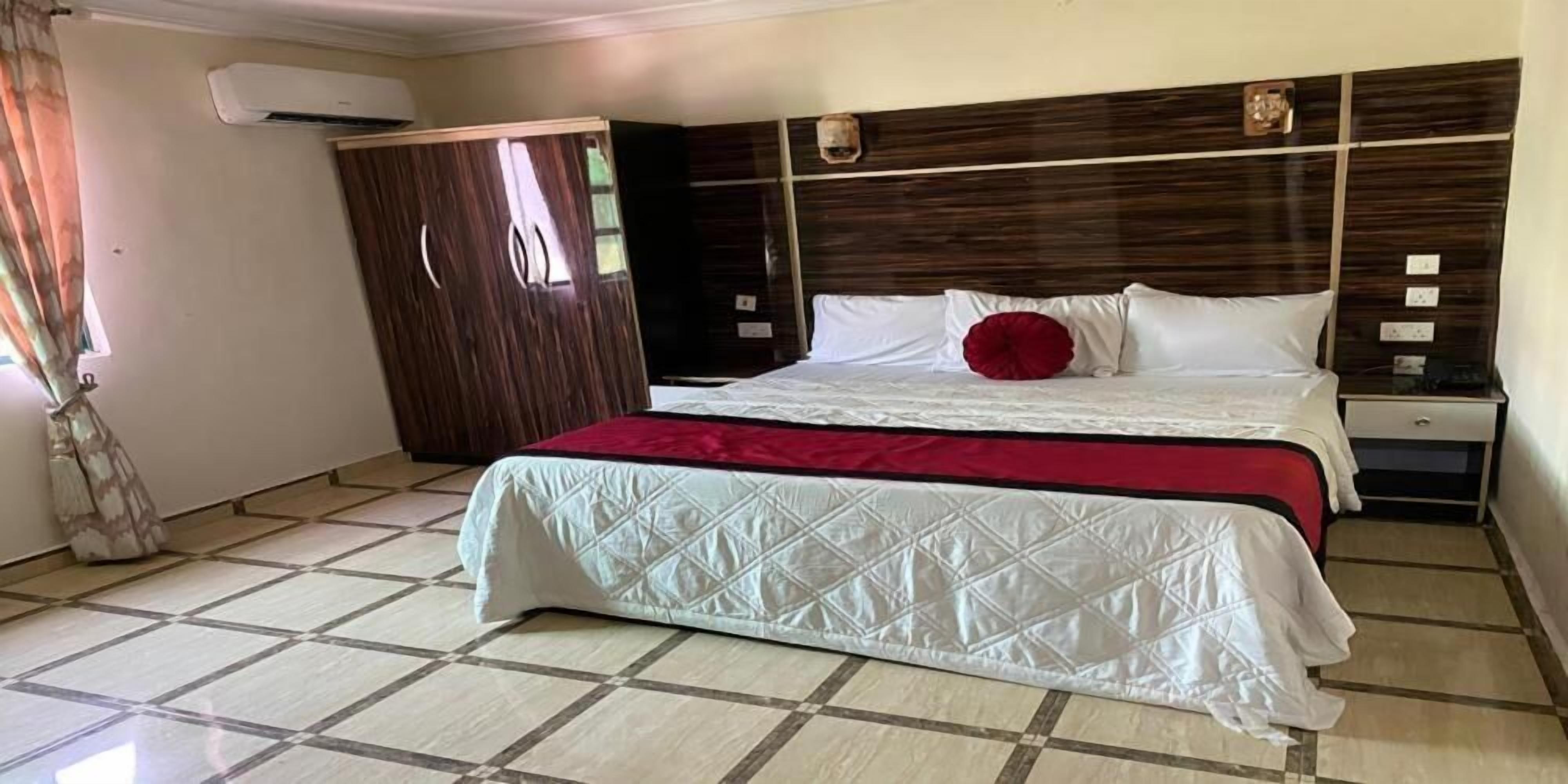 Quarto de hotel com cama, guarda-roupa, mesa de cabeceira e janela com cortinas.