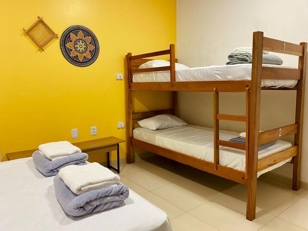 Quarto com beliche, uma mesinha pequena e um enfeite de parede decorativo.