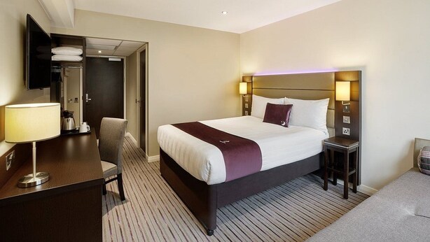 Quarto de hotel com uma cama grande, mesas de cabeceira, uma escrivaninha com luminária e uma cadeira.
