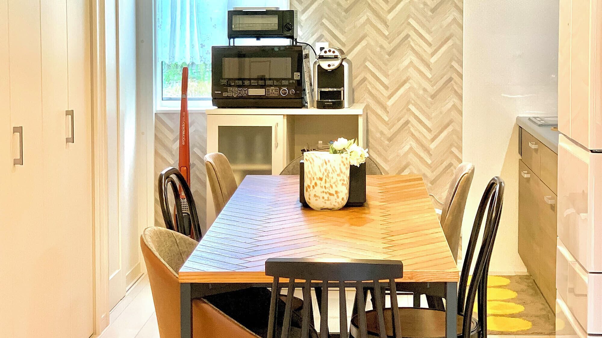 Uma sala de jantar com mesa de madeira, cadeiras e micro-ondas.