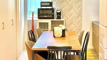 Uma sala de jantar com mesa de madeira, cadeiras e micro-ondas.