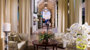 Um saguão de hotel com um sofá, uma mesa com um vaso de flores e vista para a área externa.