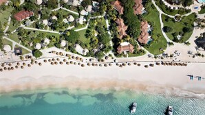 Vista aérea de um resort com praia, palmeiras e vários barcos na água.