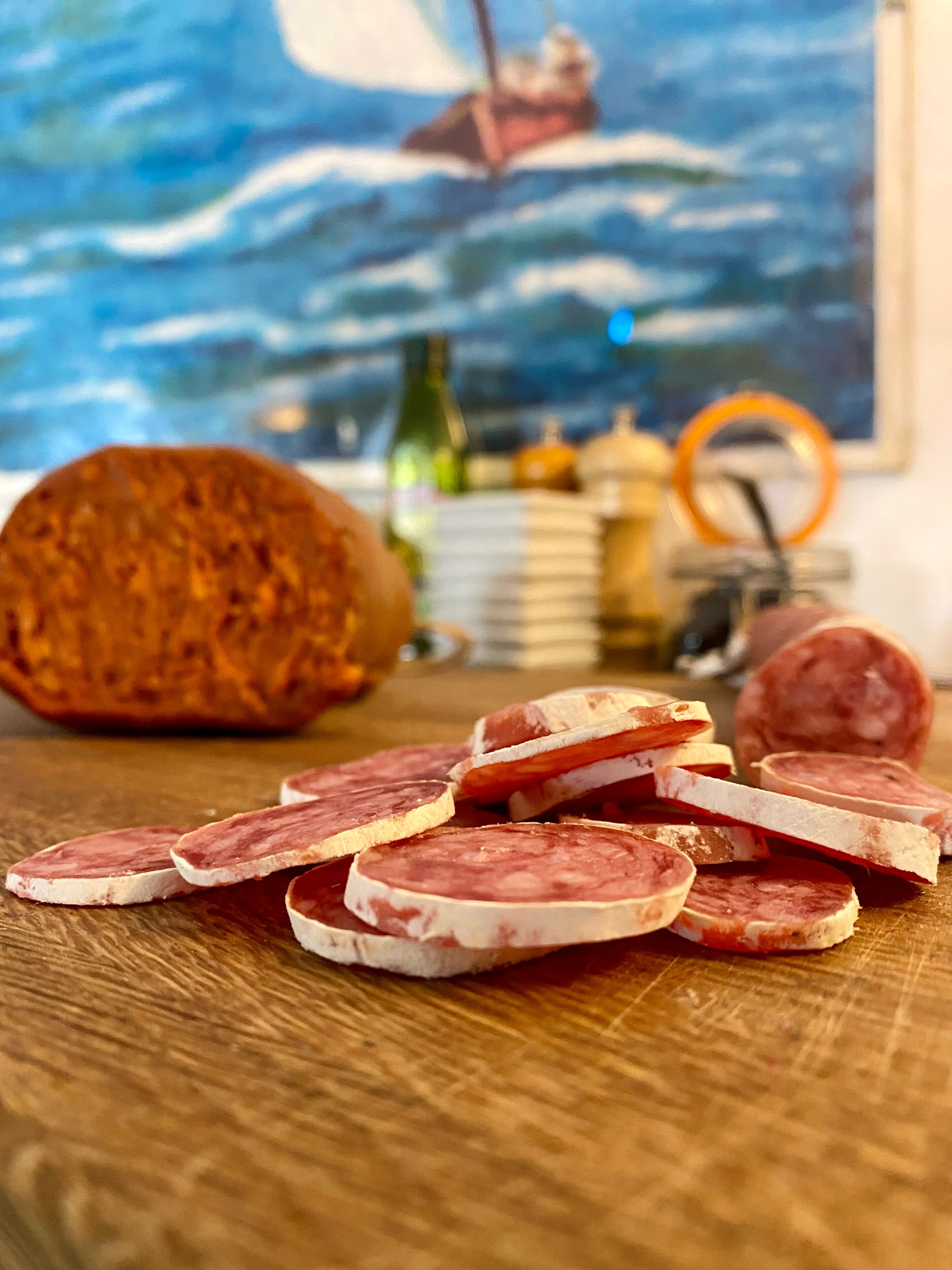 Fatias de salame em tábua de madeira, um pão e uma garrafa de azeite.