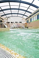Piscina interior com teto de vidro, uma fonte de água e borda revestida com azulejos.