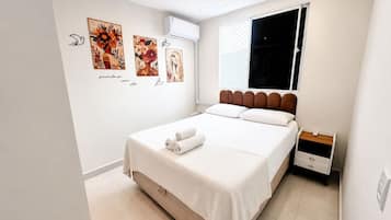 Quarto com cama, mesa de cabeceira, janela e decoração na parede.