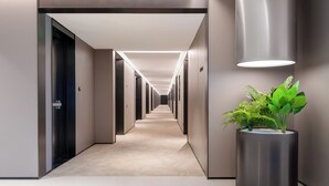 Um corredor moderno com uma planta, um aparelho de luz e uma porta no final.