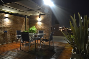 Um pátio externo com parede de tijolos, uma mesa com cadeiras e um vaso de planta.