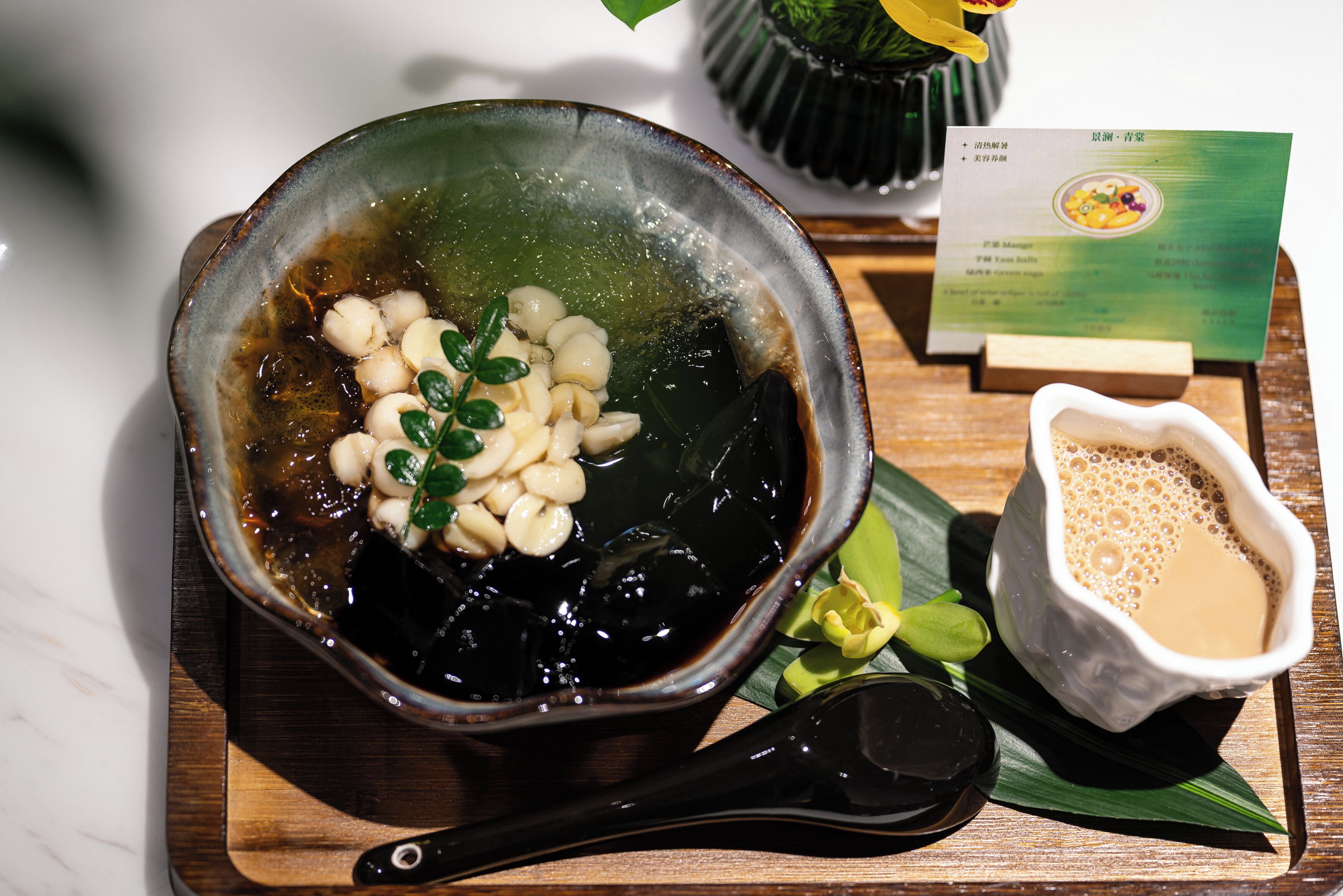 Uma tigela de sopa com uma colher e uma chávena de chá sobre um tabuleiro de madeira.