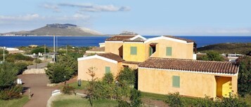 Um edifício costeiro com telhado em telhas e vista para o mar e uma montanha ao fundo.