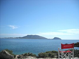 Uma cadeira de praia com uma placa vermelha com a inscrição 'SALVATAGGIO', com vista para um mar calmo e montanhas ao longe.