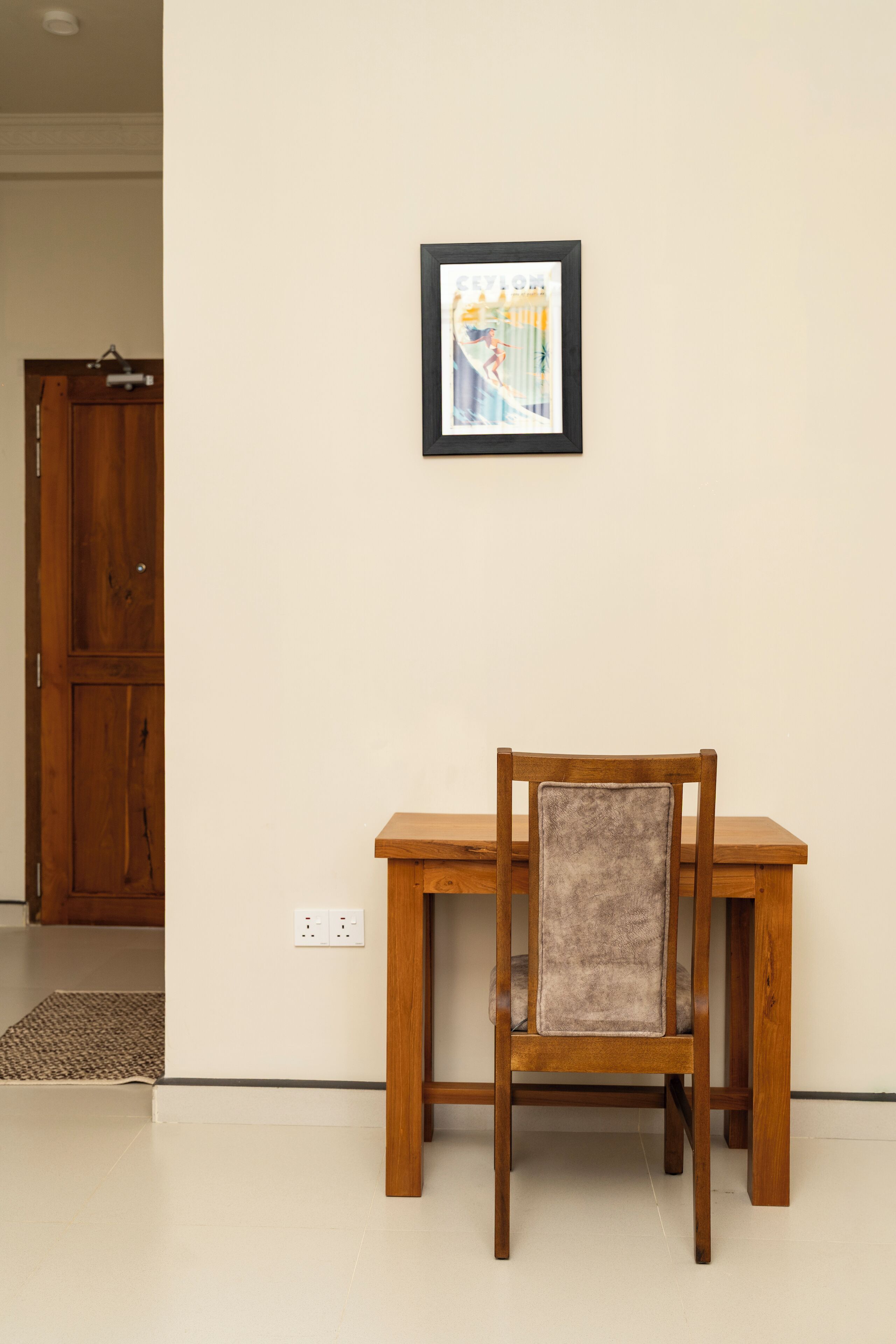 Uma mesa de madeira com uma cadeira, um quadro na parede e uma porta de madeira ao fundo.