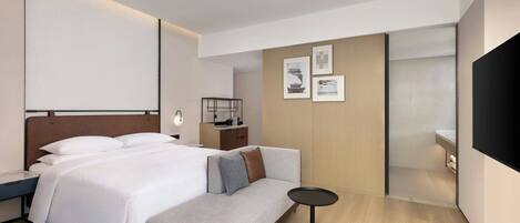 Quarto de hotel moderno com cama, sofá, mesinha e televisão.
