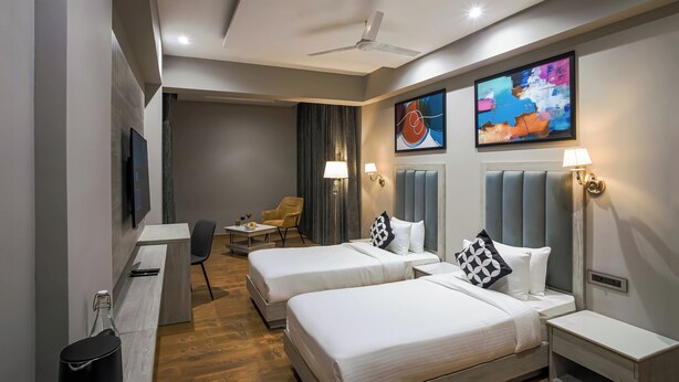 Quarto de hotel com duas camas, uma escrivaninha, uma cadeira, televisão e obras de arte nas paredes.