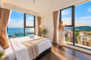 Quarto de hotel com uma cama grande, vista para o mar e para a cidade.