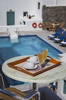 Uma mesa à beira da piscina com uma bandeja de itens de café da manhã, incluindo xícaras, um copo de suco de laranja e um copo de água.