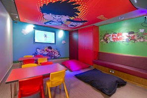 Uma sala de recreação infantil com móveis coloridos, um mural de desenho animado e um letreiro com a inscrição 'FUN TIME'.