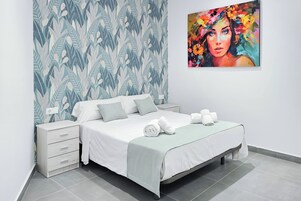 Quarto moderno com cama, mesas de cabeceira brancas e parede com padrão de folhagem.