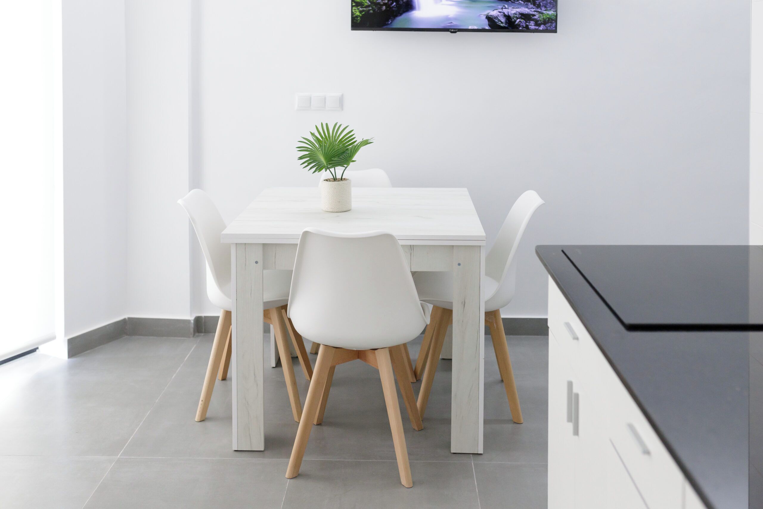 Uma área de refeições moderna com uma mesa e cadeiras brancas, uma planta em vaso e uma televisão de tela plana na parede.