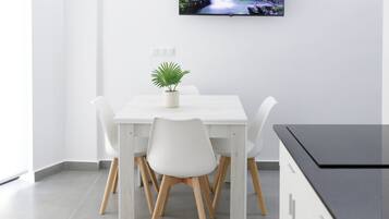 Uma área de refeições moderna com uma mesa e cadeiras brancas, uma planta em vaso e uma televisão de tela plana na parede.