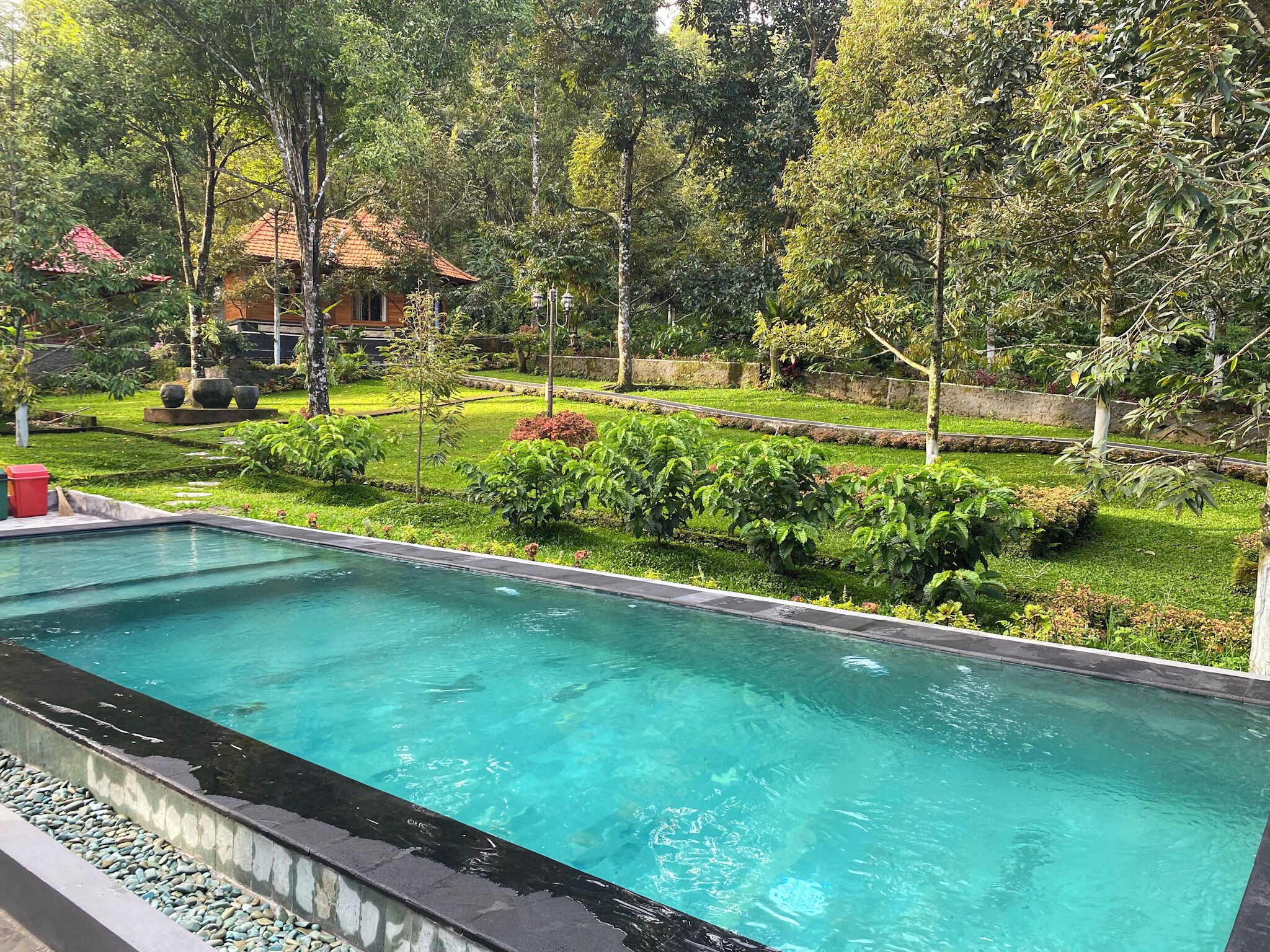 Piscina com jardim ao redor e um edifício com telhado vermelho.