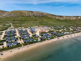 Vista aérea de um resort costeiro com várias acomodações em estilo bungalow, uma praia de areia e uma vista desobstruída do mar.