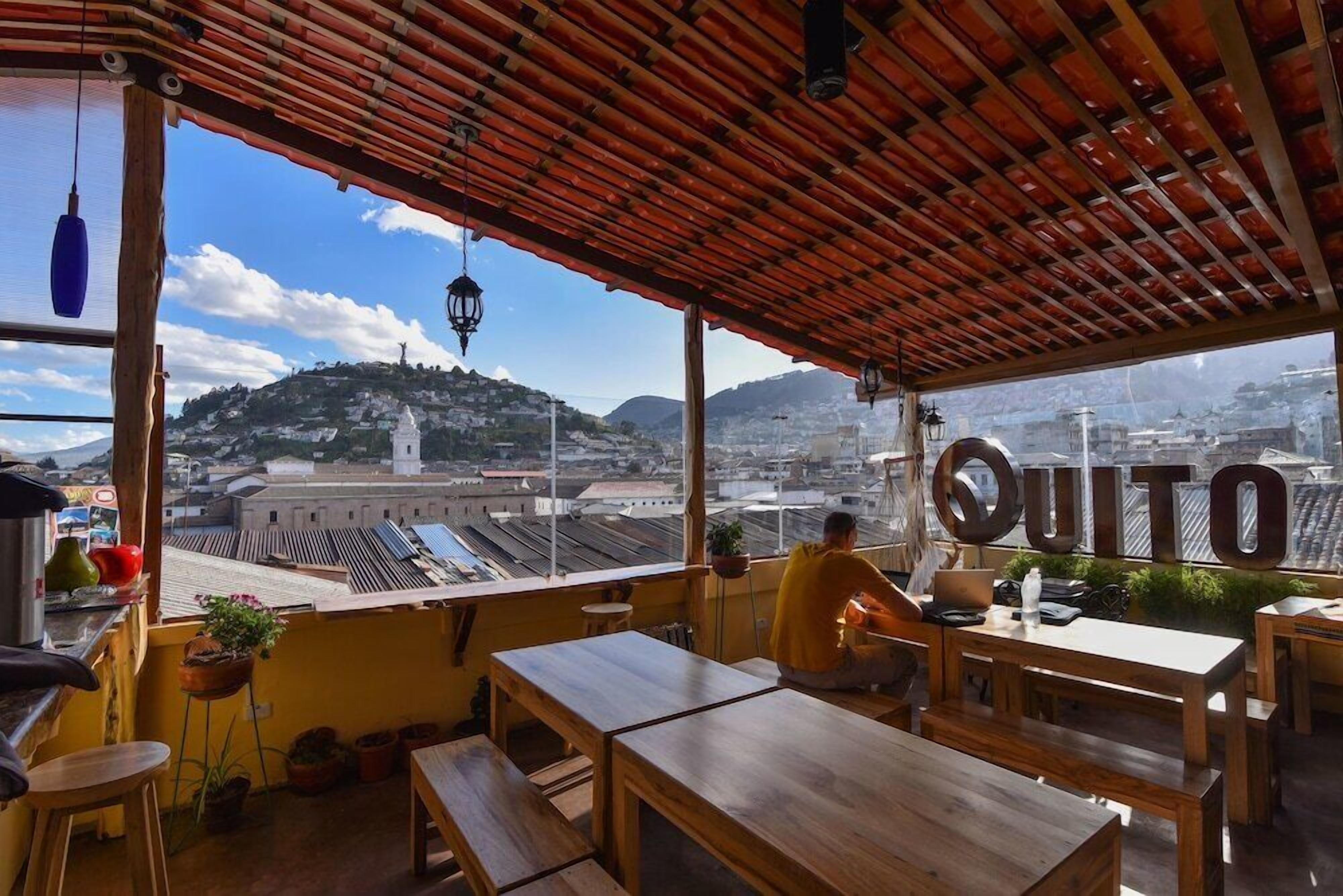 Terraço no telhado com móveis de madeira, vista do horizonte urbano de Quito e uma placa com a palavra "QUITTO".