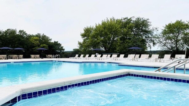 Piscina com espreguiçadeiras e guarda-sóis, cercada por árvores.